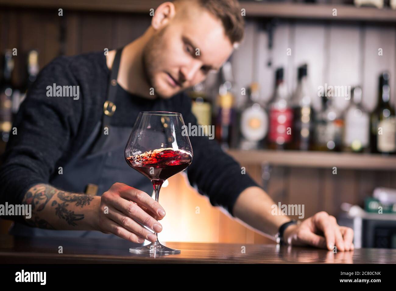 Focused young male sommelier in suite looking at red wine in glass over ...