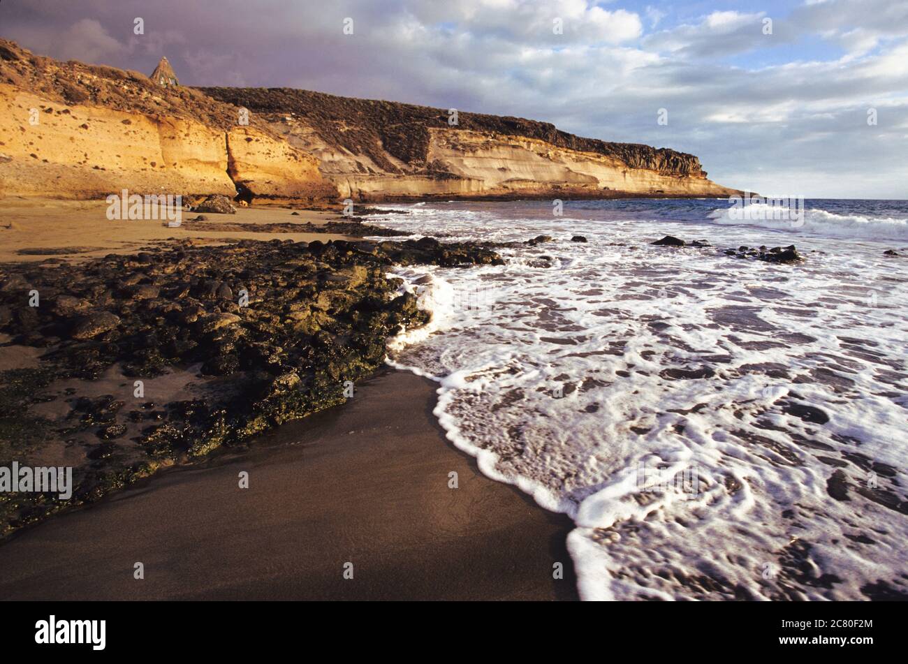 Vertical shot of ocean water receding from the sandy shore with a rock ...