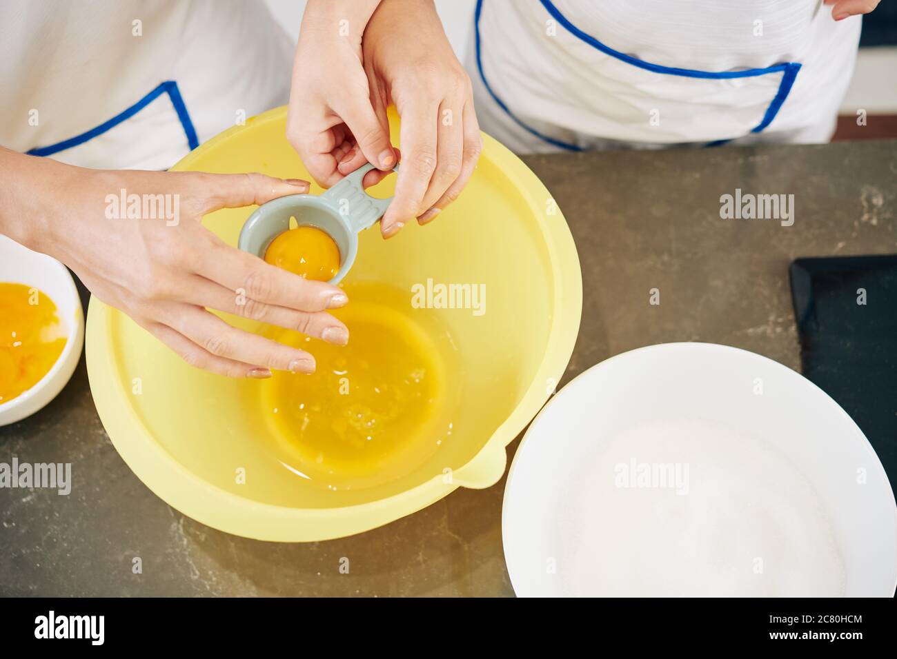 Hands of mother showing daughter how to use plastic tool when separating egg yolks from egg ...