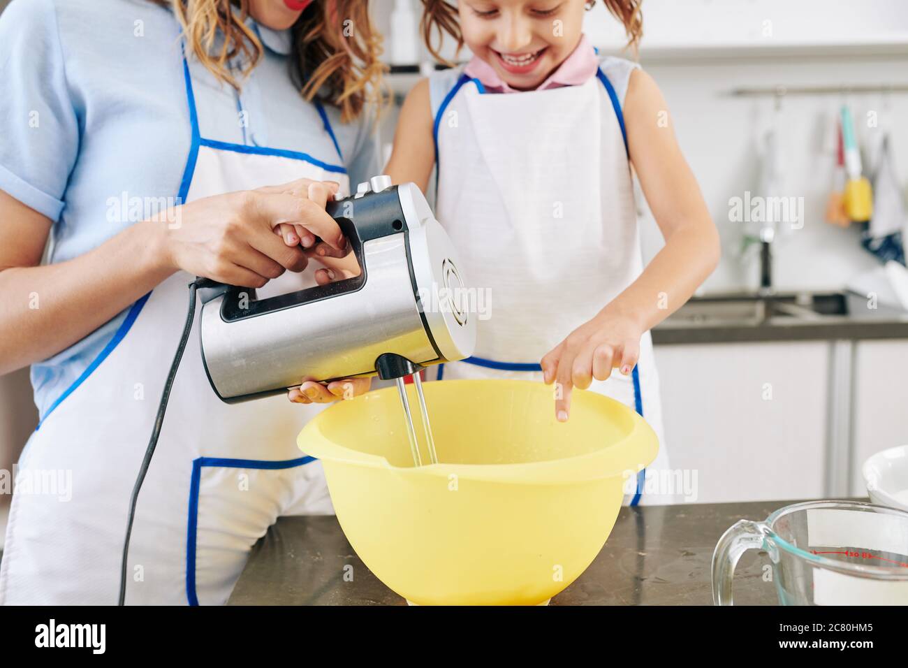 Happy little girl and her mother mixing pancake dough in big plastic ...