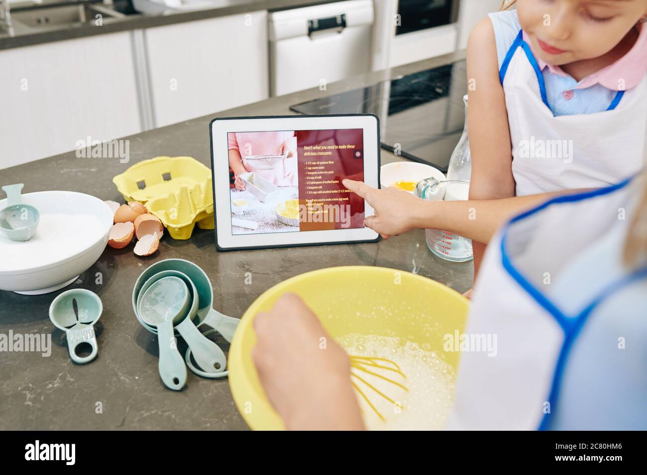 Woman pointing at recipe on screen of tablet computer when baking cake ...