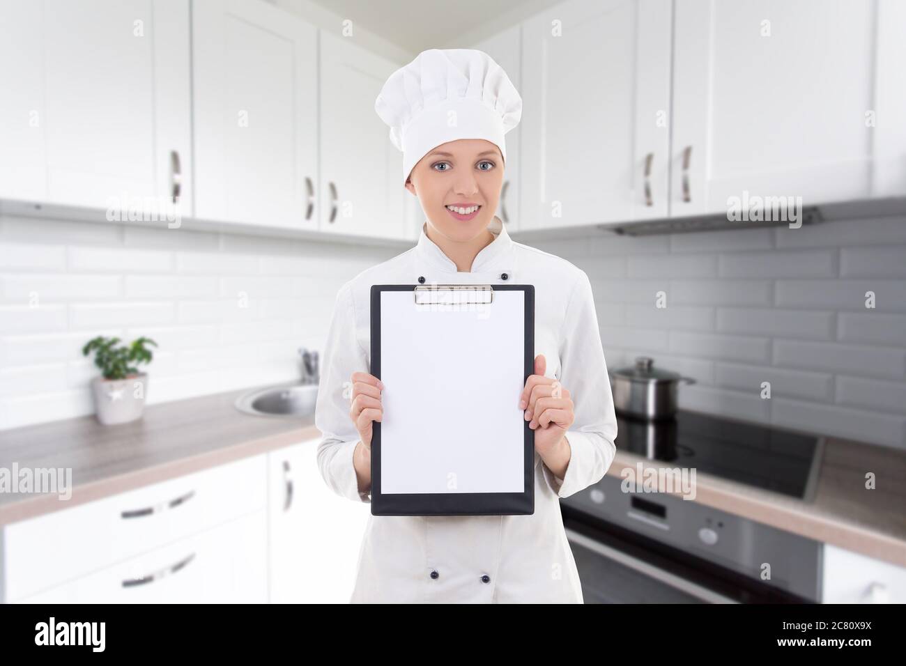 young woman chef in uniform holding clipboard with blank paper in ...