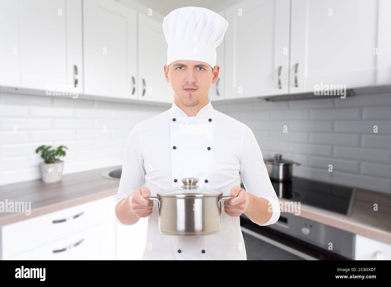 young man chef in uniform with saucepan in modern kitchen Stock Photo ...