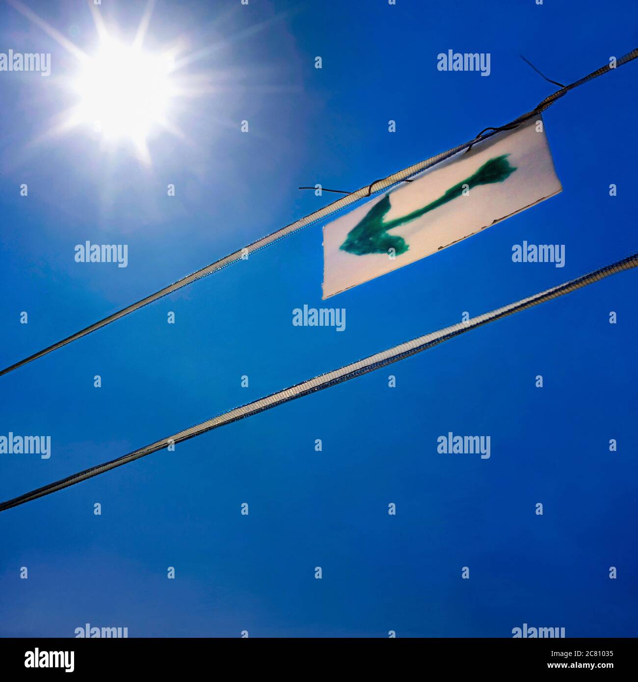 Bright blue sky with sun and directional arrow sign hanging on wires in ...