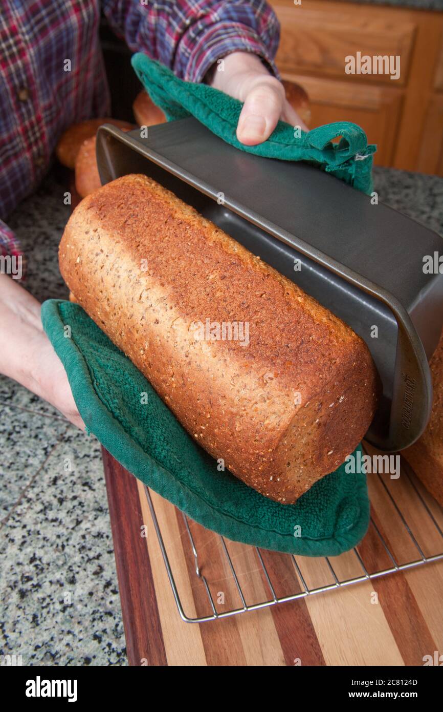 Woman removing loaf of just baked multigrain bread from bread pan Stock ...