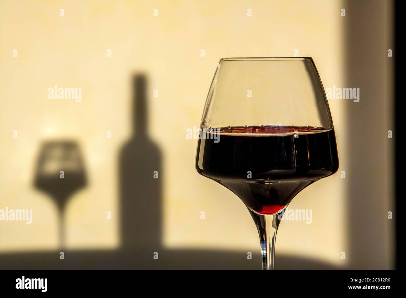 Glass of red wine placed on a table casting a shadow of a wine bottle ...