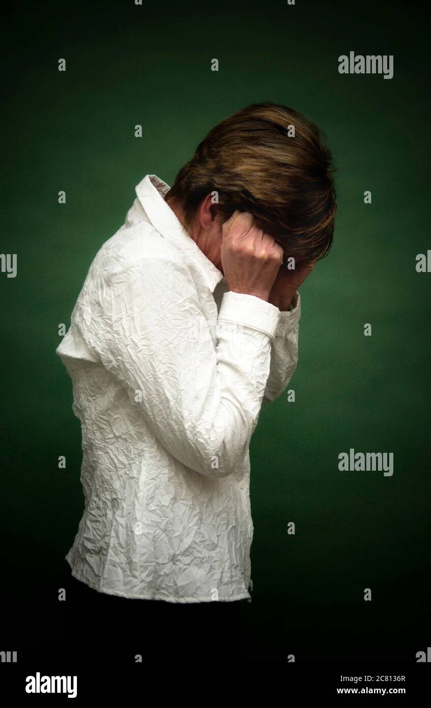 Woman with distressed expression covering her face in a dimly lit room ...
