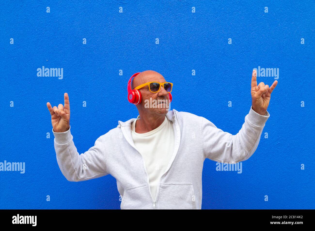 senior man listen music and have fun making rock gesture on blue ...