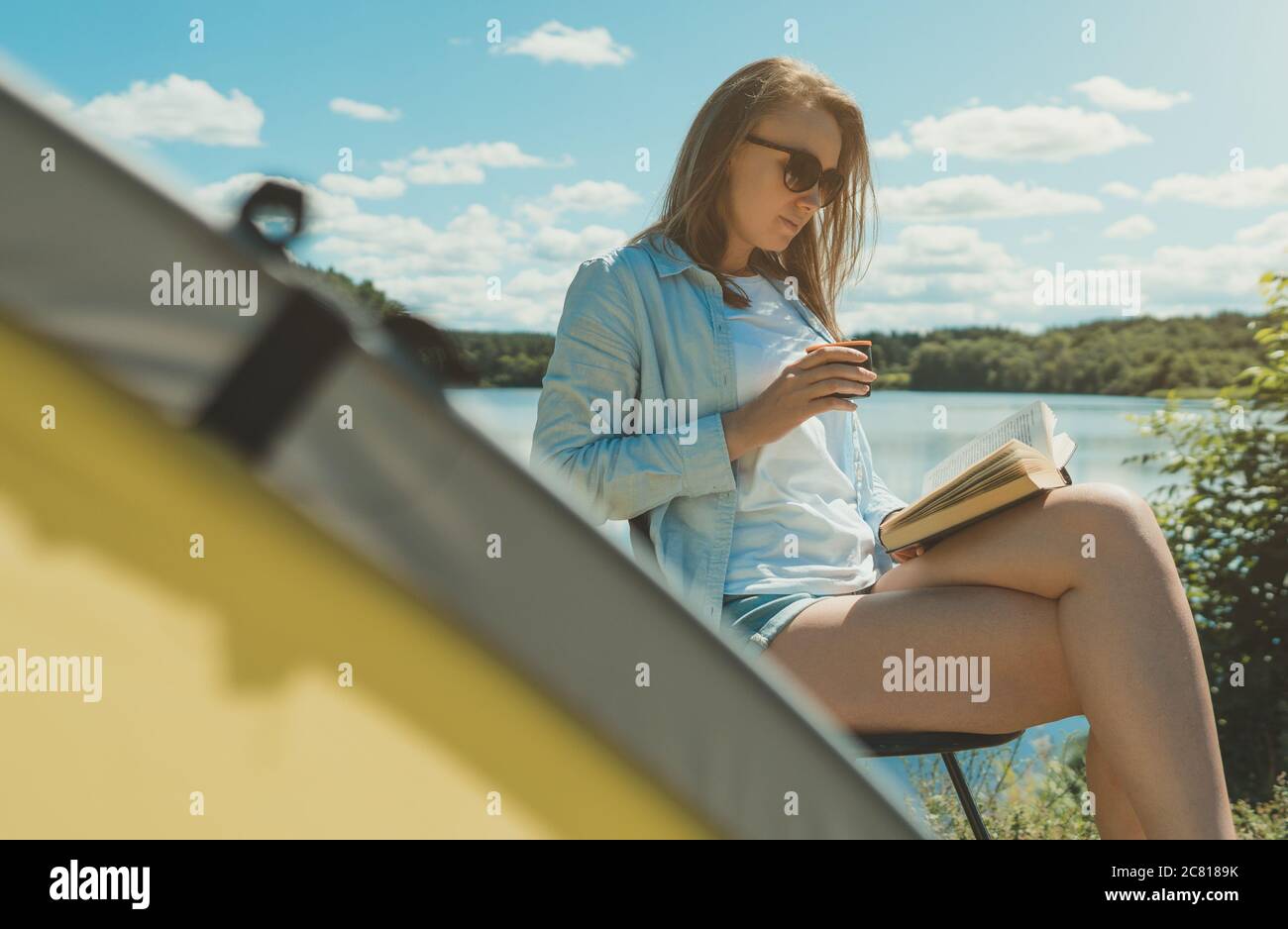 Woman reading a book near camping tent by the lake Stock Photo - Alamy