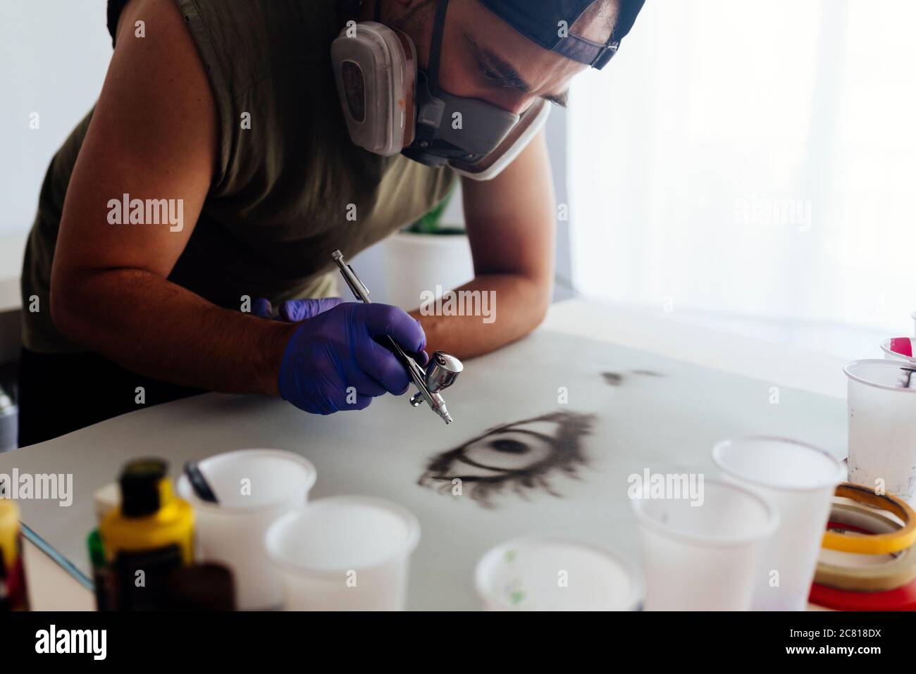 Close up of airbrush painter with mask drawing an eye on a paper Stock ...