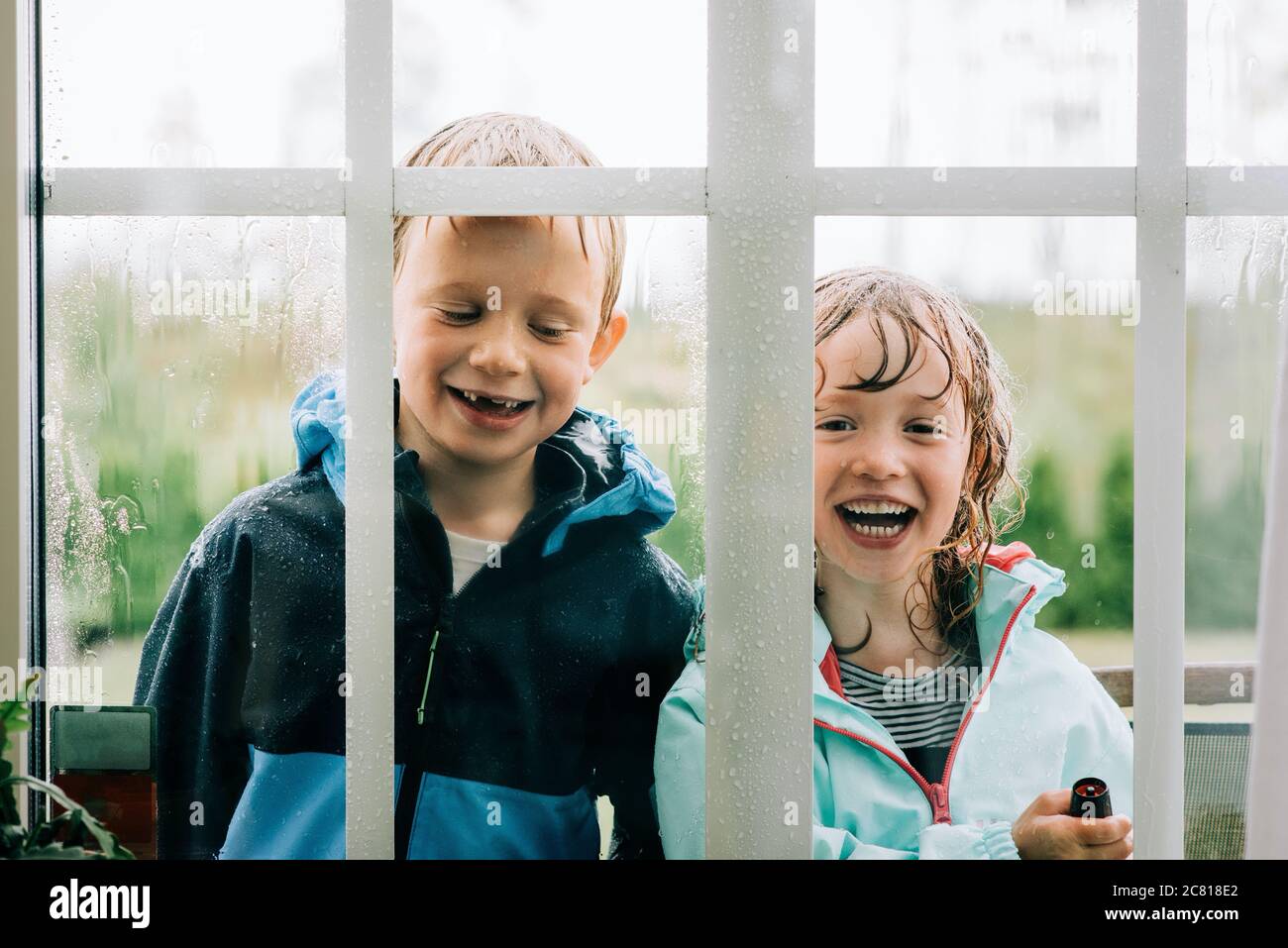 brother and sister looking through a window laughing whilst playing ...