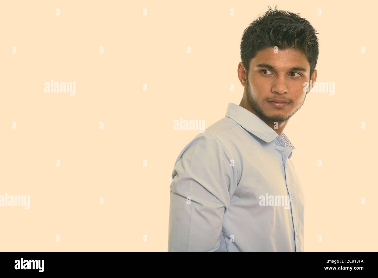 Studio shot of young handsome Indian man thinking while looking back ...