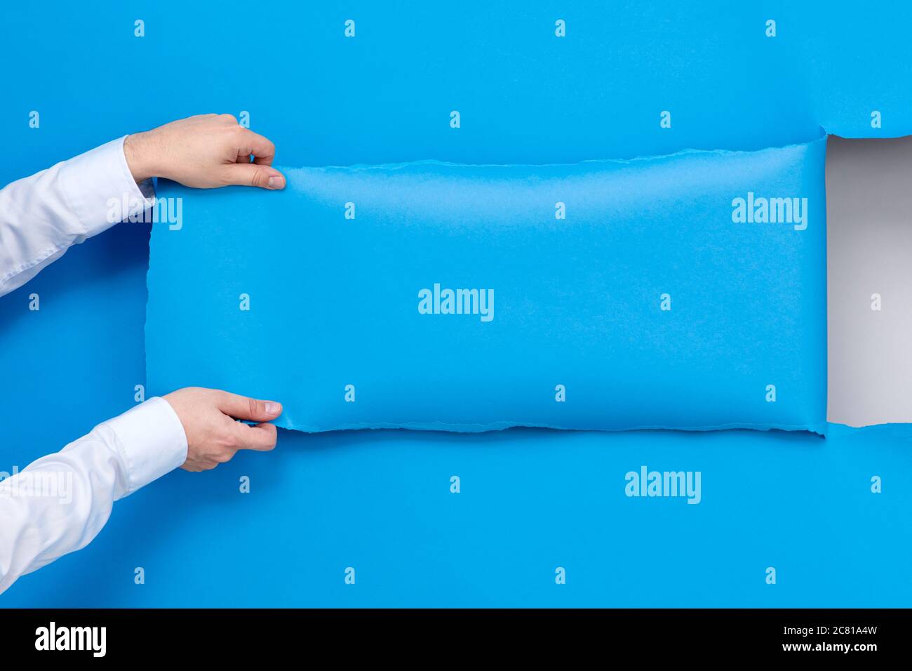 Man's hands tears up blue paper background with blue copy space for ...