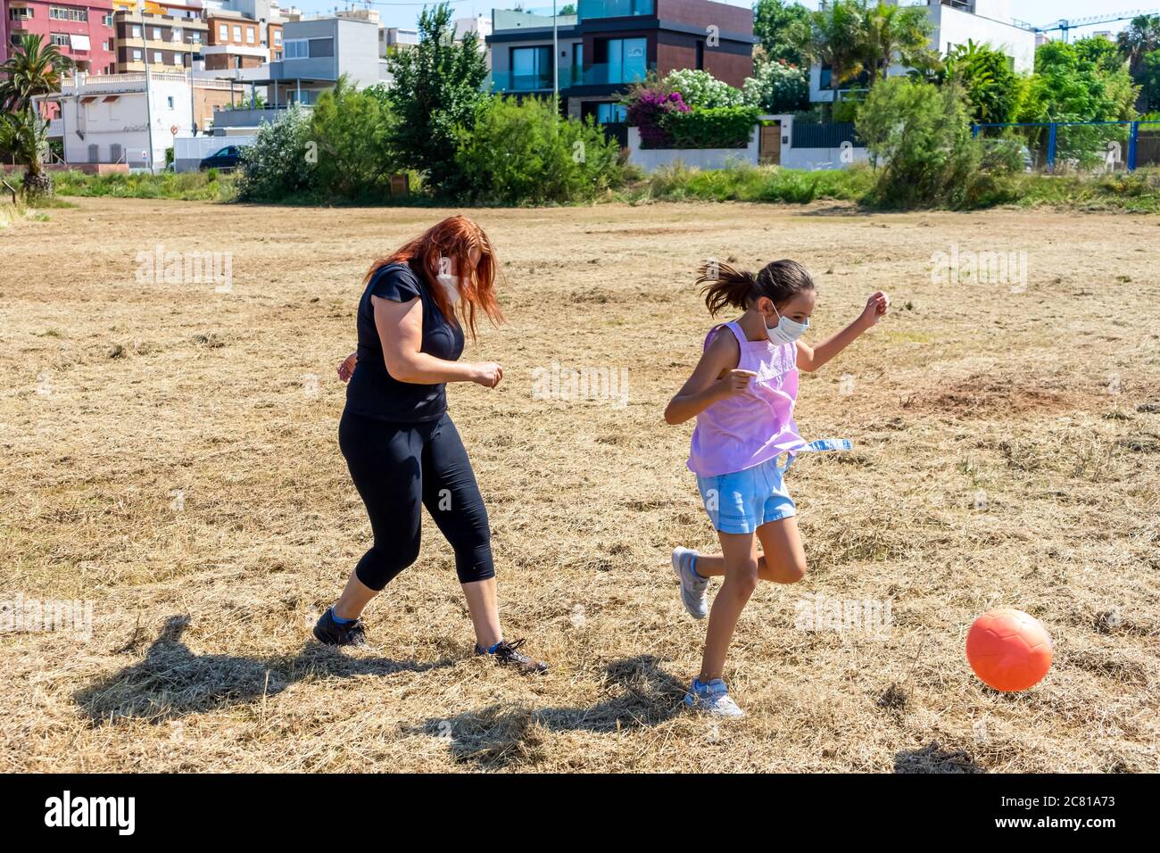 Mother and daughter playing soccer with an orange ball in a field with ...