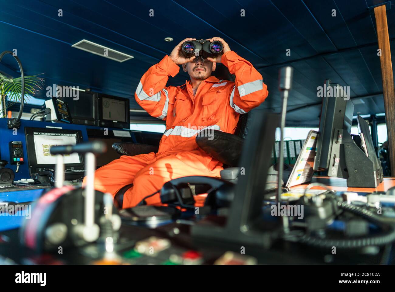 Filipino deck Officer on bridge of vessel or ship looking through ...