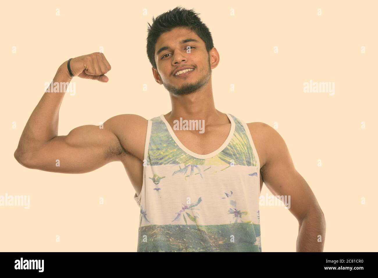 Studio shot of young happy Indian man smiling while flexing his arm and ...
