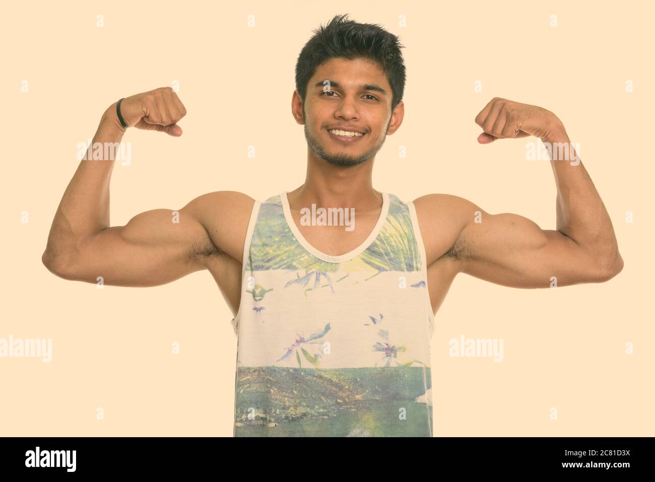 Studio shot of young happy Indian man smiling while flexing both arms ...