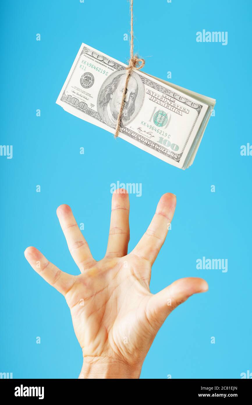 A hand tries to grab a wad of money on a rope on a blue background ...