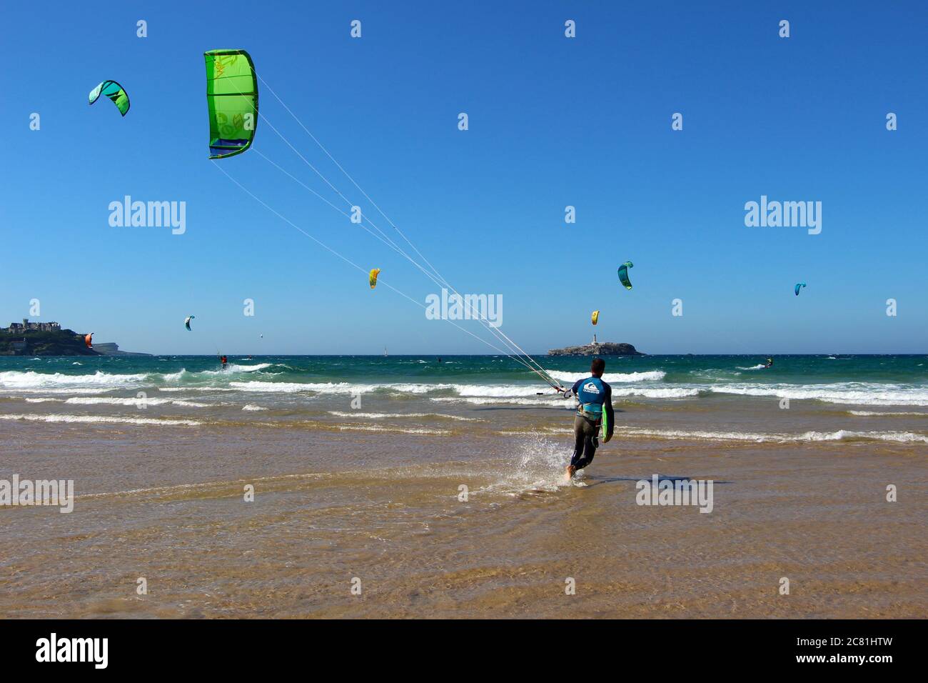 Kitesurfer or kiteboarder walking with flying kite into the surf ...