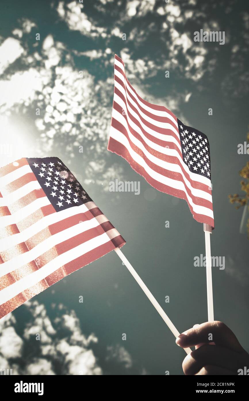 Hand holding two american flags on the blue sky with sunlight ...