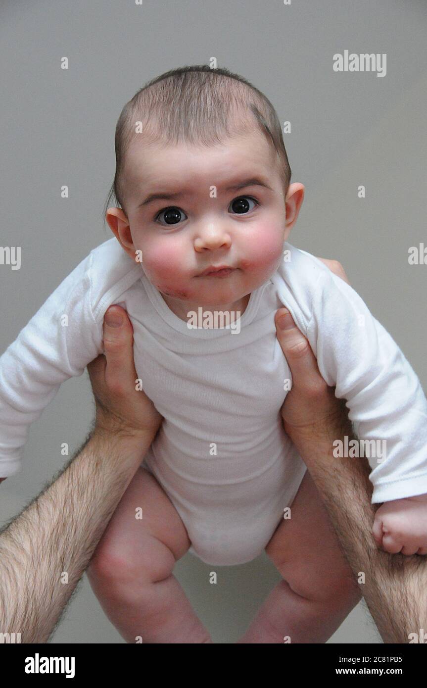 An adorable male baby is being help up by his father's hands while he ...
