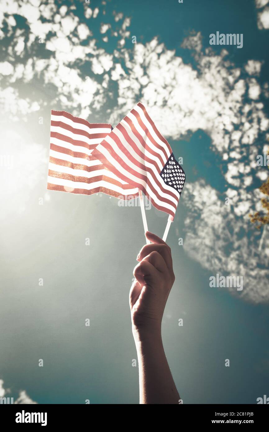 Hand holding two american flags on the blue sky with sunlight ...