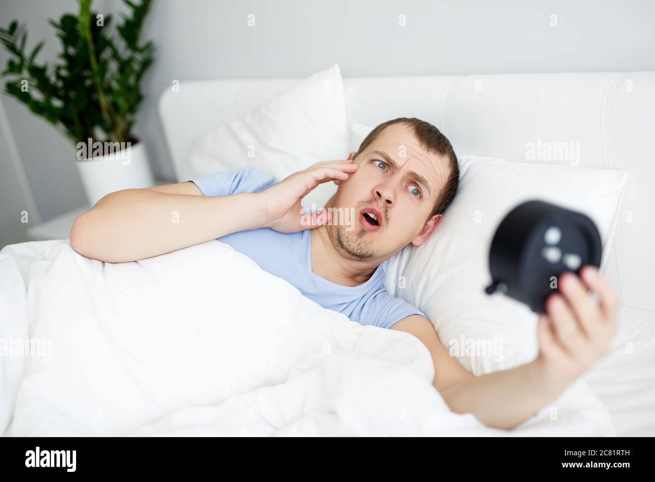 portrait of overslept shocked man looking at alarm clock lying in bed ...