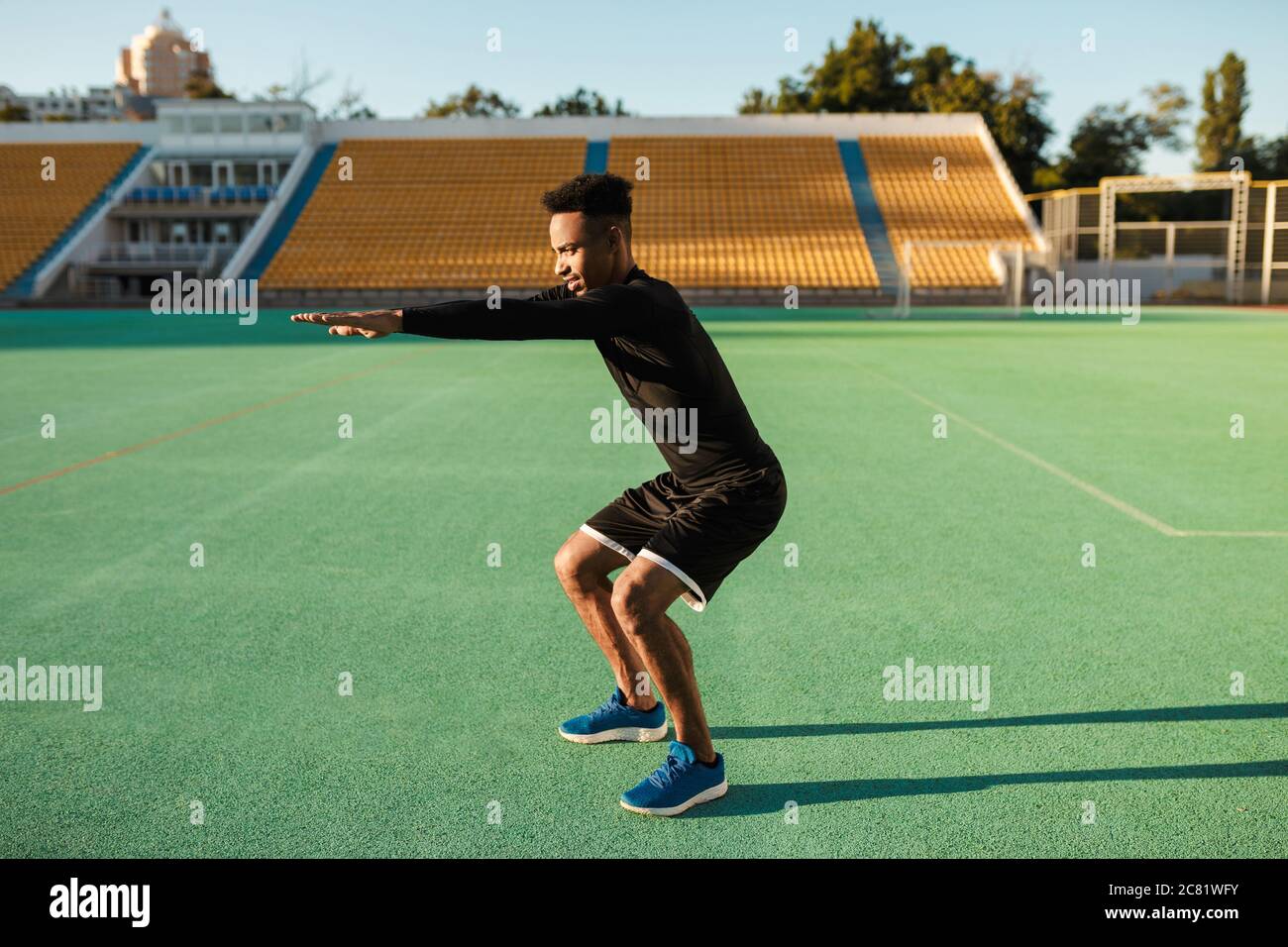 Side view of young African American sportsman squatting during workout ...