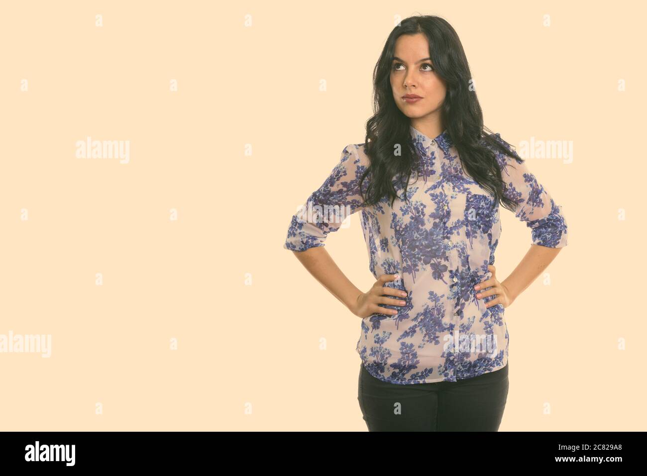 Studio shot of young beautiful Spanish woman standing while thinking ...