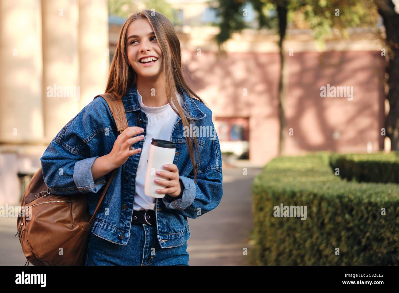 Cheerful student girl in denim jacket with backpack happily looking ...
