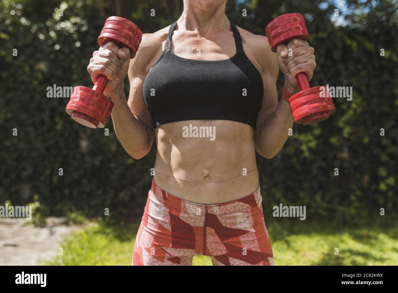 Athletic Caucasian female working out with dumbbells in a park ...