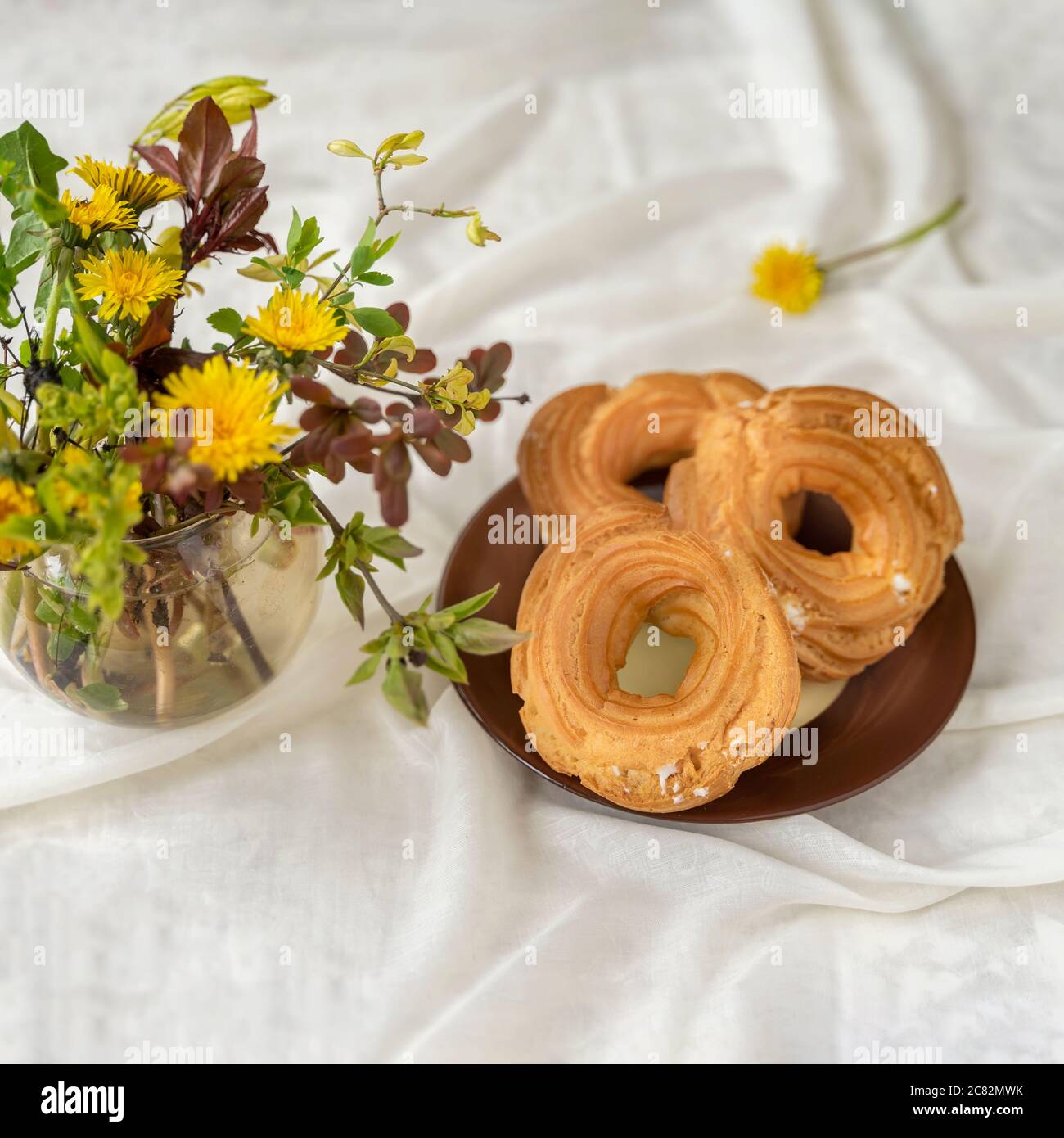 Three eclair rings on a saucer, flowers in a vase. Sweet food, bakery ...