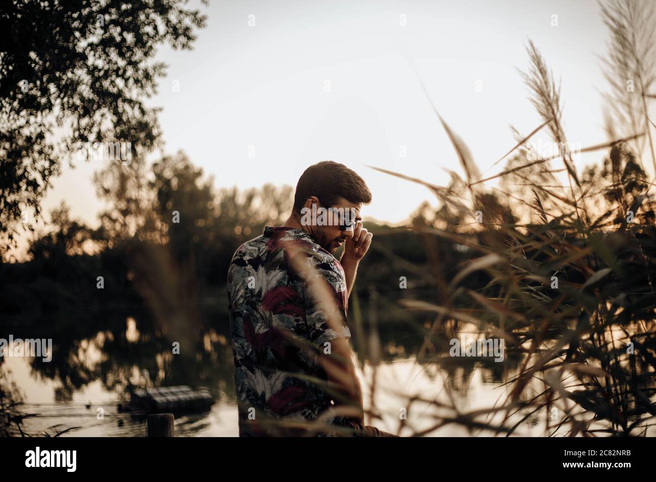 Boy looking interested in something through his sunglasses at sunset ...