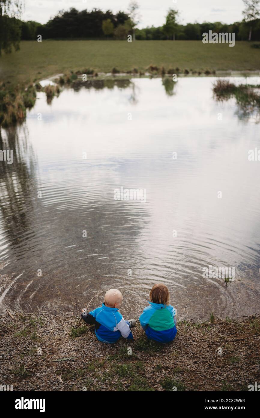 Back view of brothers in front of a lake in a park on overcast day ...