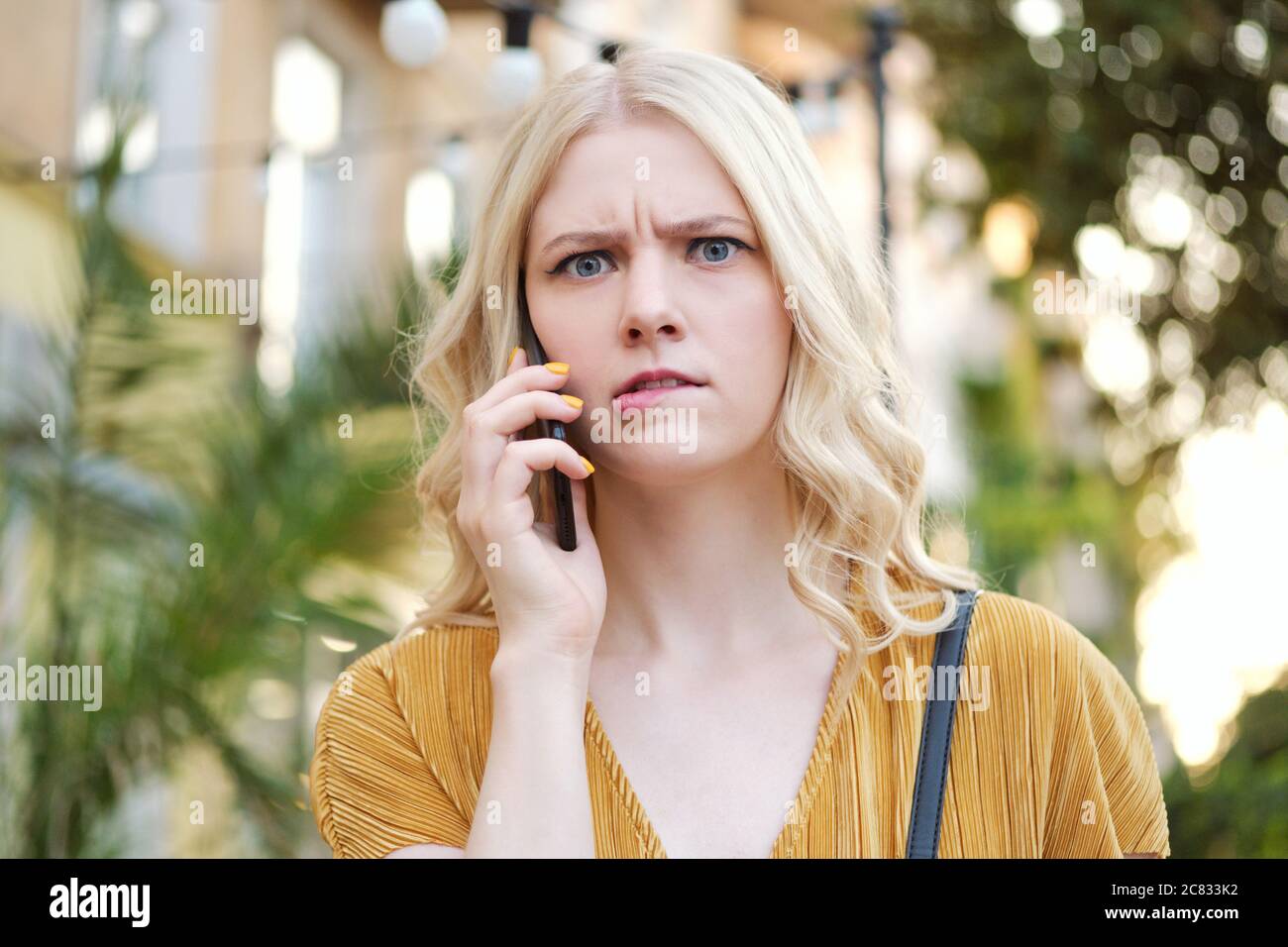 Portrait of serious blond girl biting lip and scaredly looking in ...