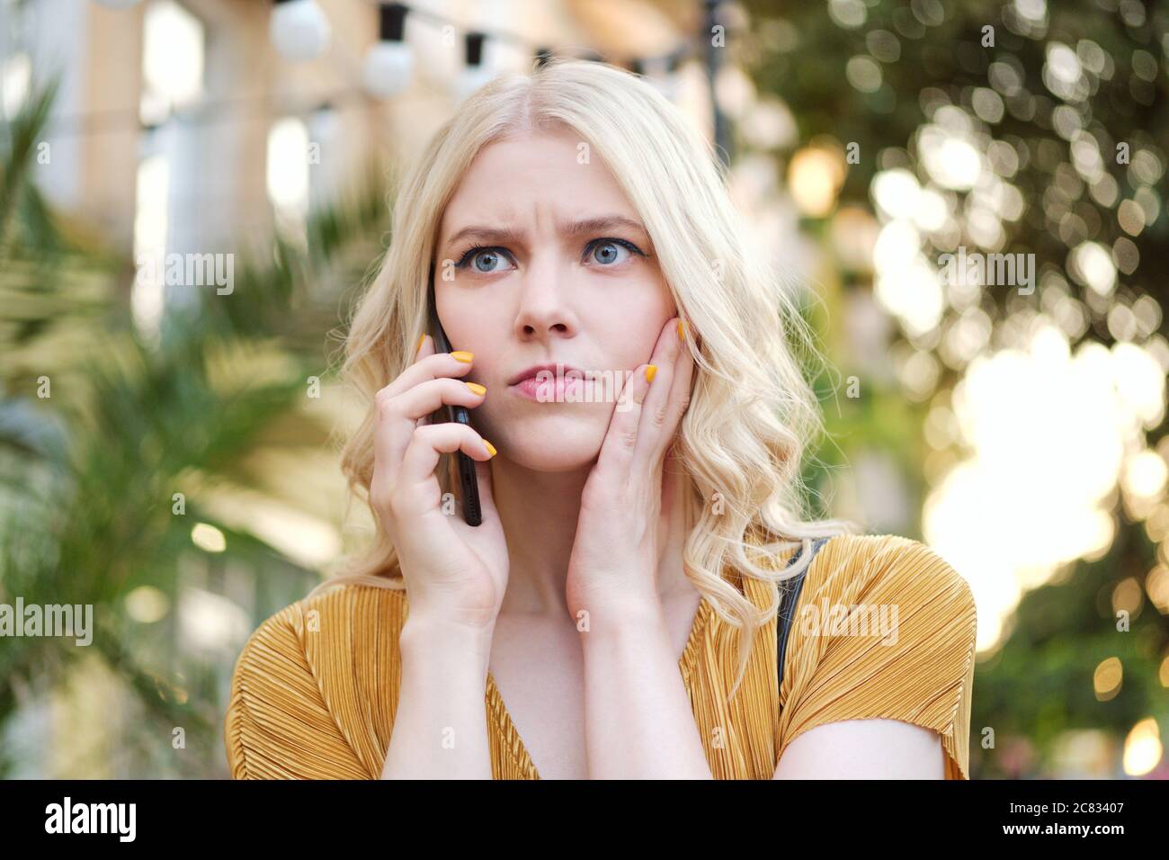Portrait of serious blond girl amazedly looking away while talking on ...