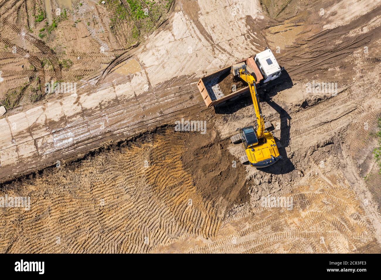 industrial excavator loading ground into a dump truck on construction site. aerial top view ...