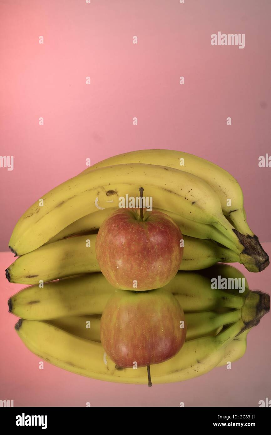 A bunch of bananas and apples on mirroring table on mirror red ...