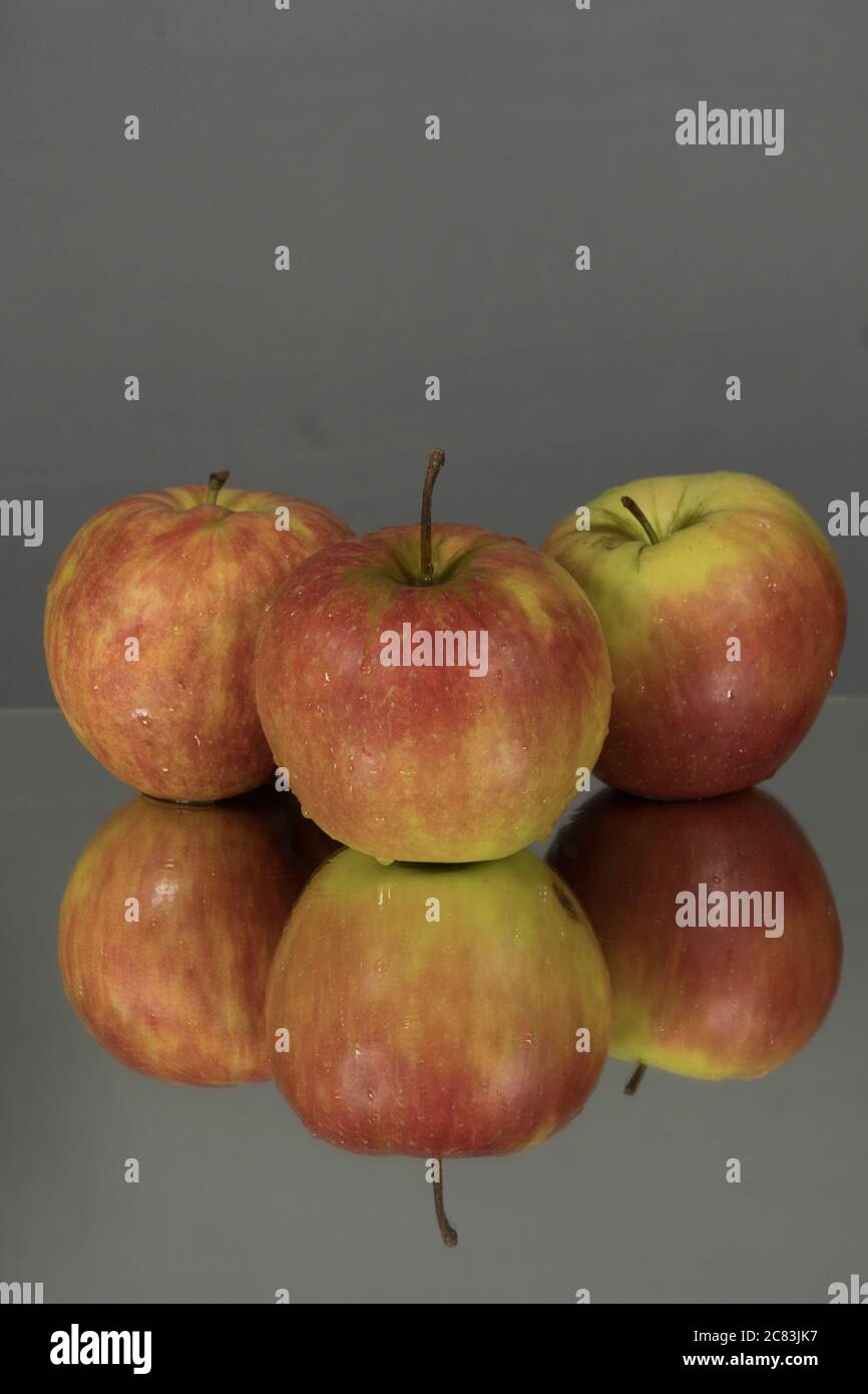 Three red apples on mirroring table on mirror gray background with ...