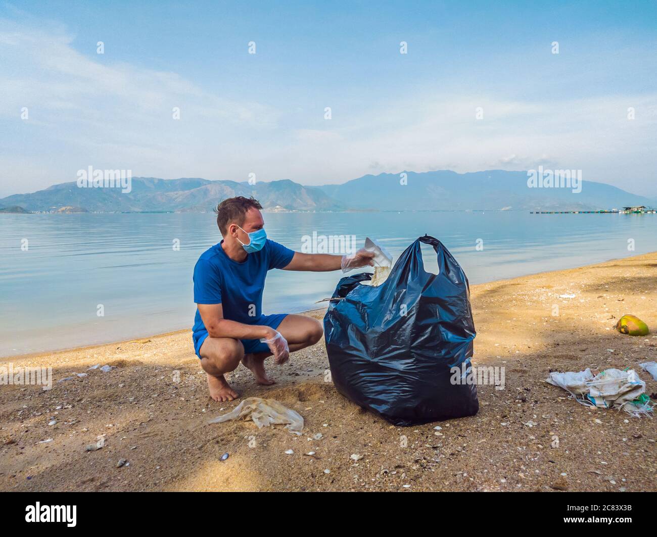 Man in gloves pick up plastic bags that pollute sea. Problem of spilled ...