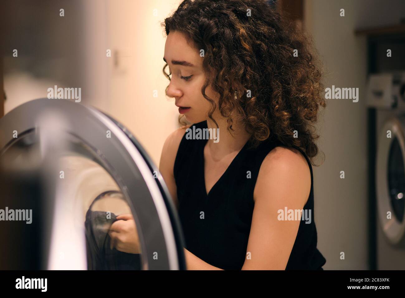 Portrait of attractive brunette girl thoughtfully loading clothes into ...