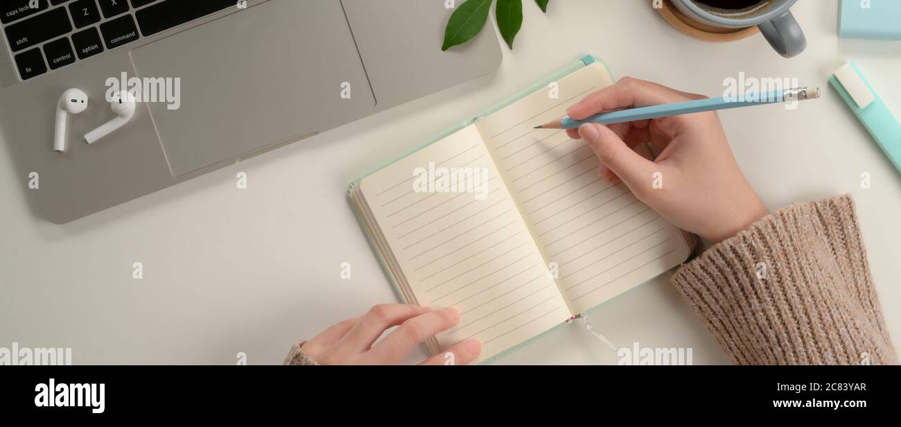 Overhead shot of female student taking note on blank notebook while ...