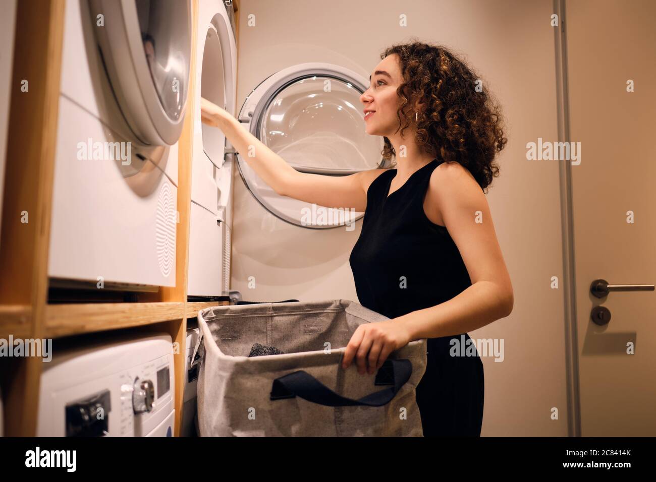 Attractive brunette girl dreamily loading clothes into washing machine ...