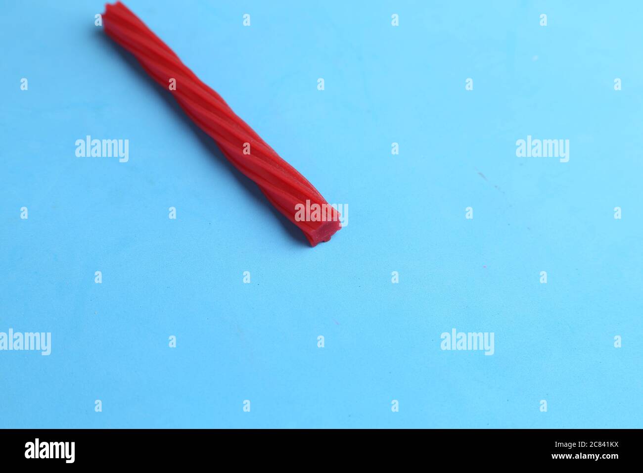 Single long red twisted candy on a blue background Stock Photo - Alamy