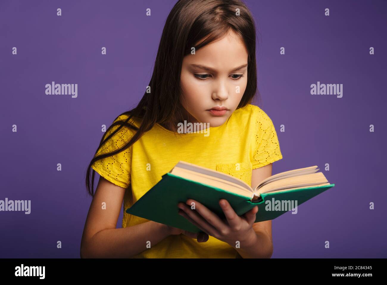 Photo of smart focused girl posing and reading book on camera isolated ...