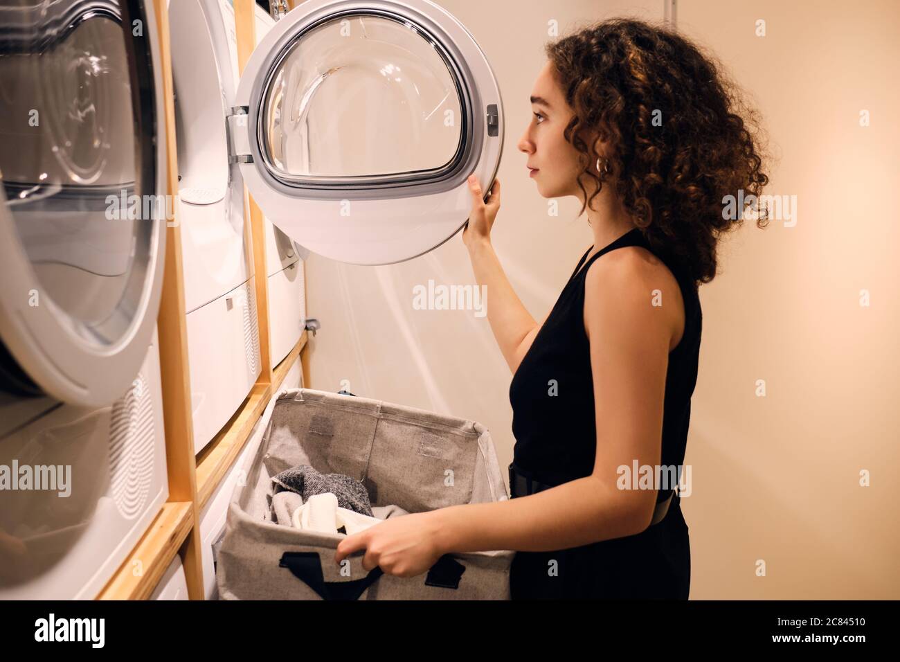 Beautiful girl loading clothes into washing machine in modern self ...