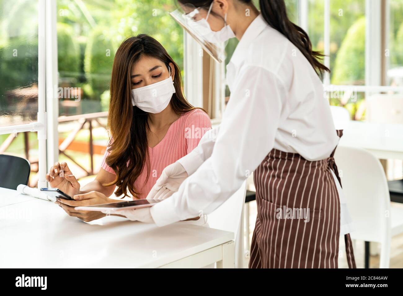 Asian waitress wear facemask and face shield using tablet to show ...