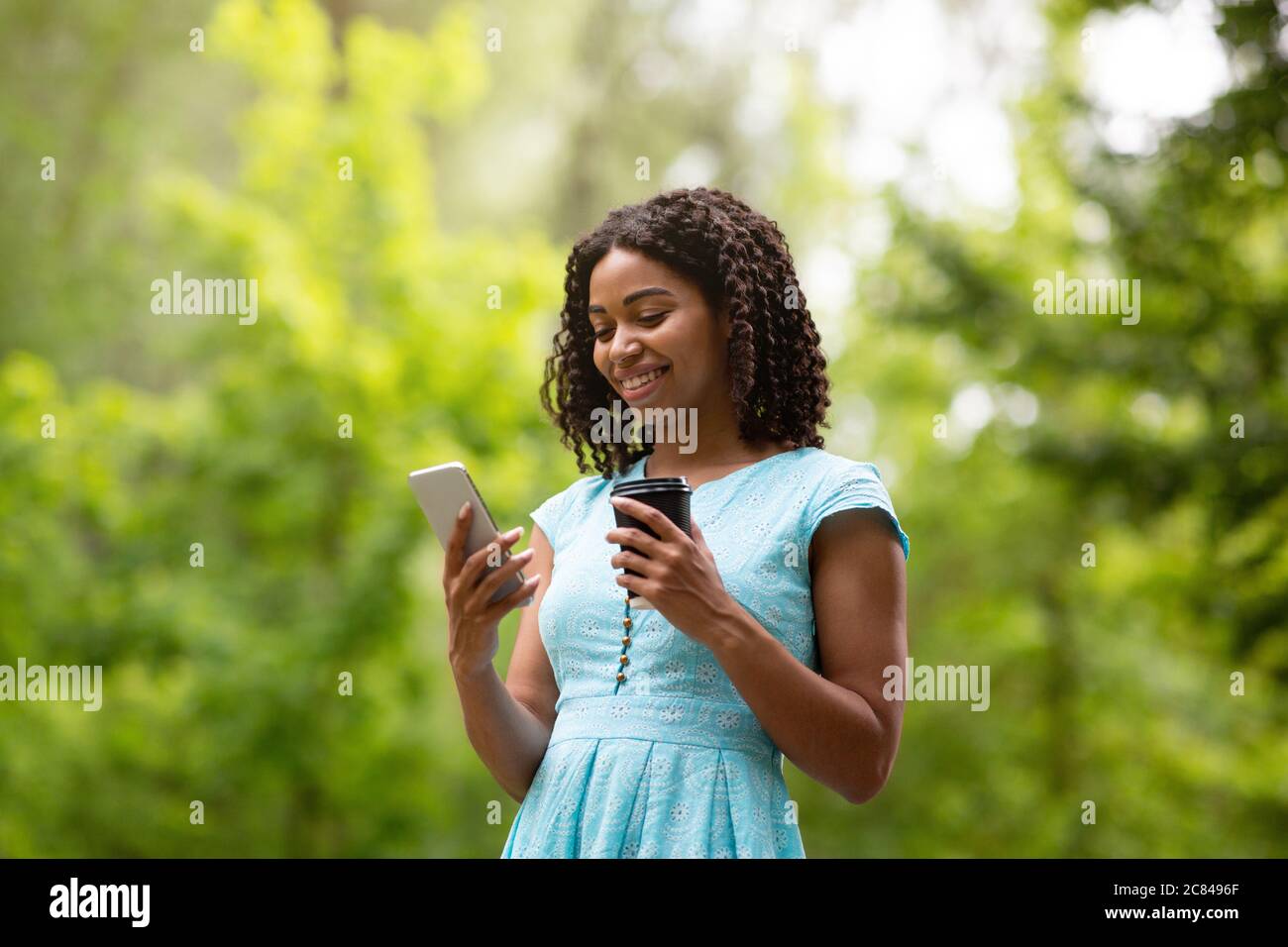 Lovely black lady with takeout coffee browsing social media on ...