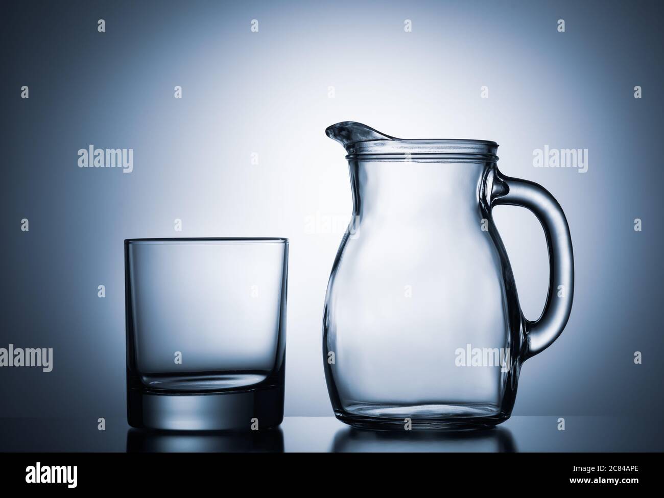 Empty water glass with water jug against blue illuminated background ...