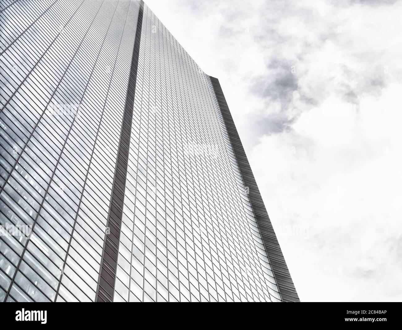 Low angle shot of a modern glass skyscraper on a cloudy sky background ...